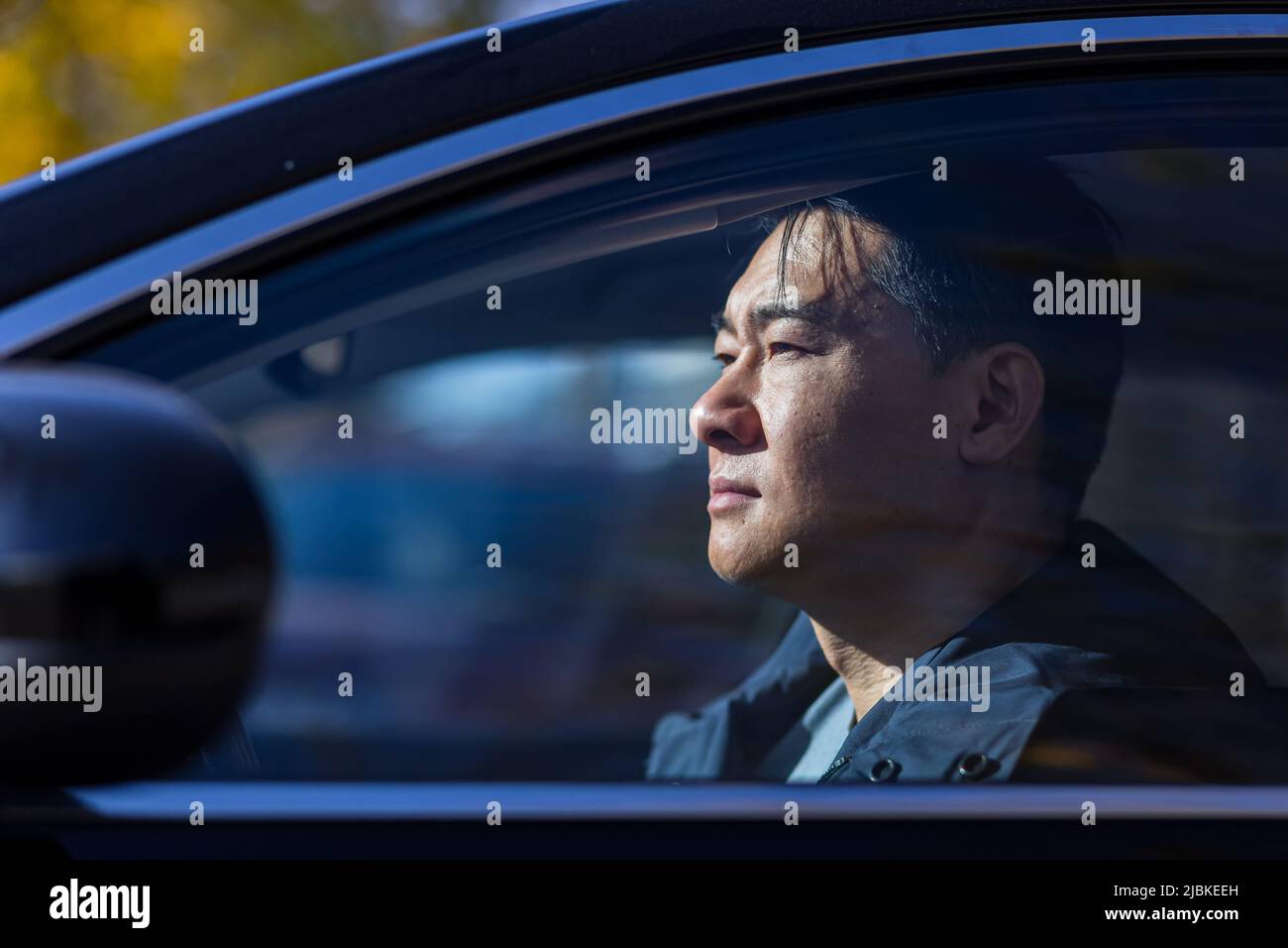 A pensive Asian man is sitting in the car, the driver is waiting and ...
