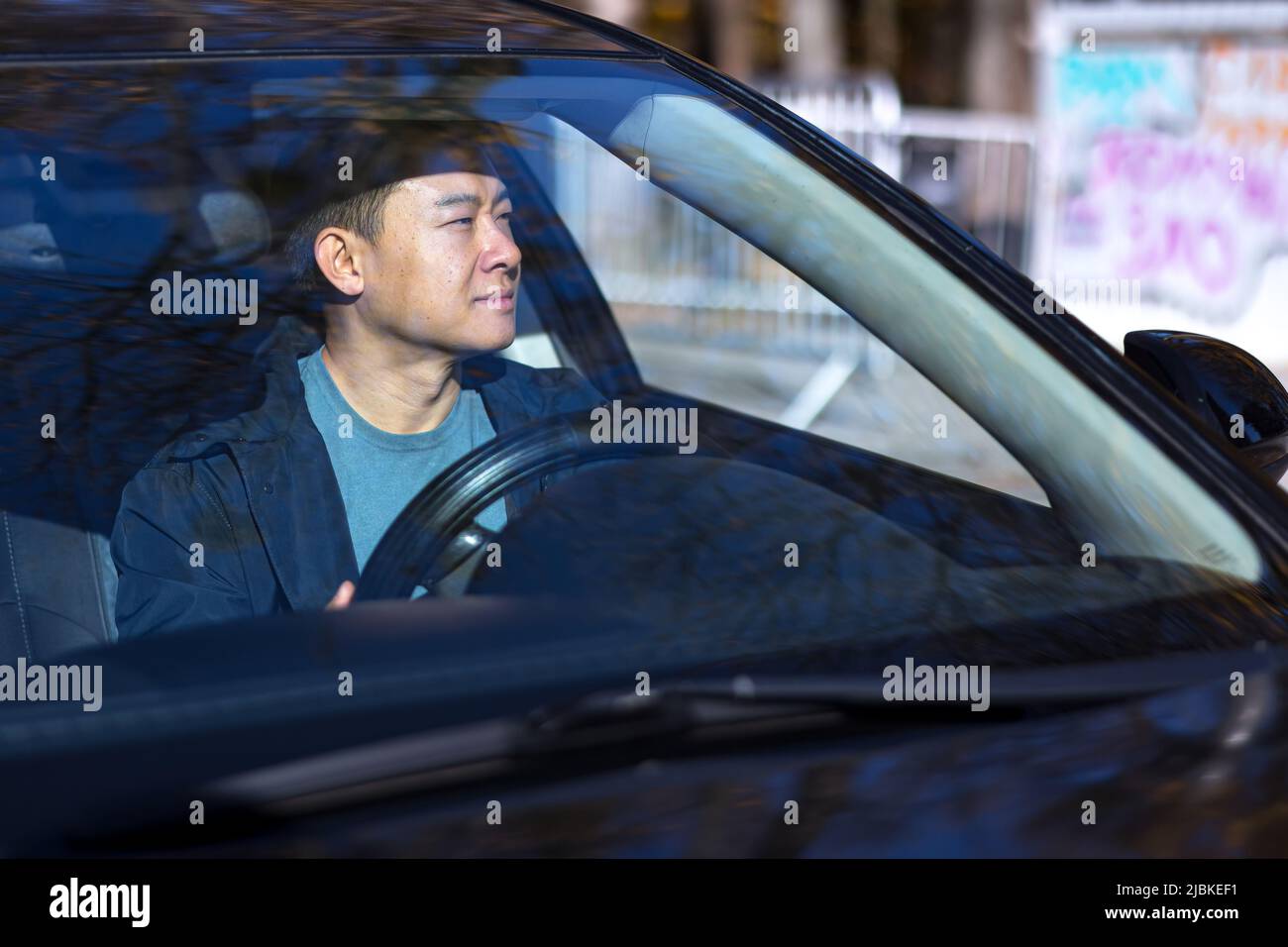A pensive Asian man is sitting in the car, the driver is waiting and ...