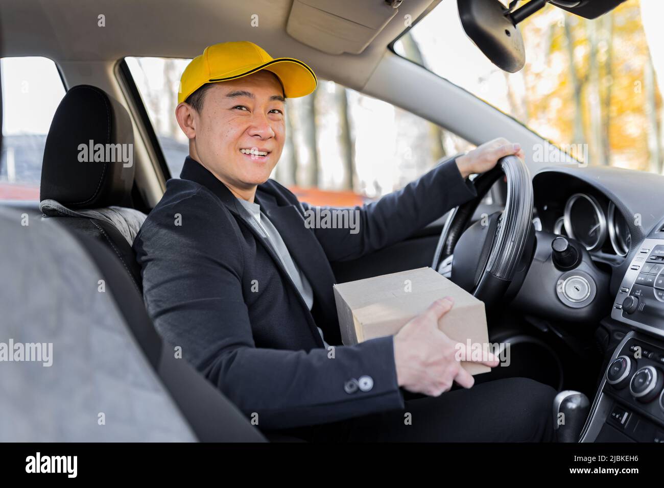 Male courier asian looks into the camera and smiles holding a parcel ...