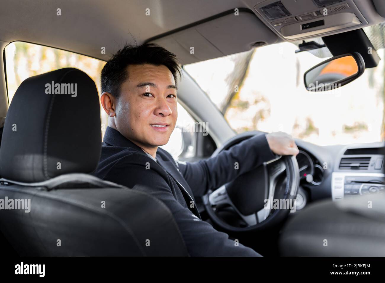 A man driving an Asian car behind the wheel looks at the camera and ...