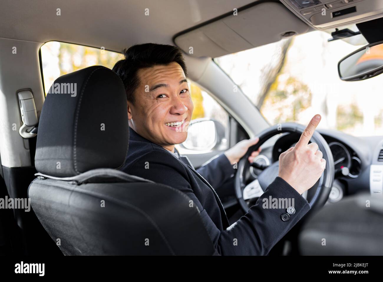 A man driving an Asian car behind the wheel looks at the camera and ...