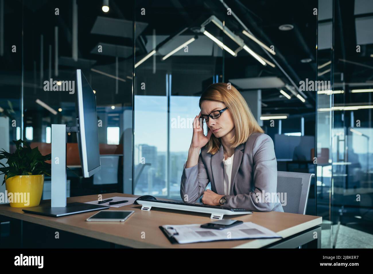 Senior business woman has a severe headache while working in a modern ...