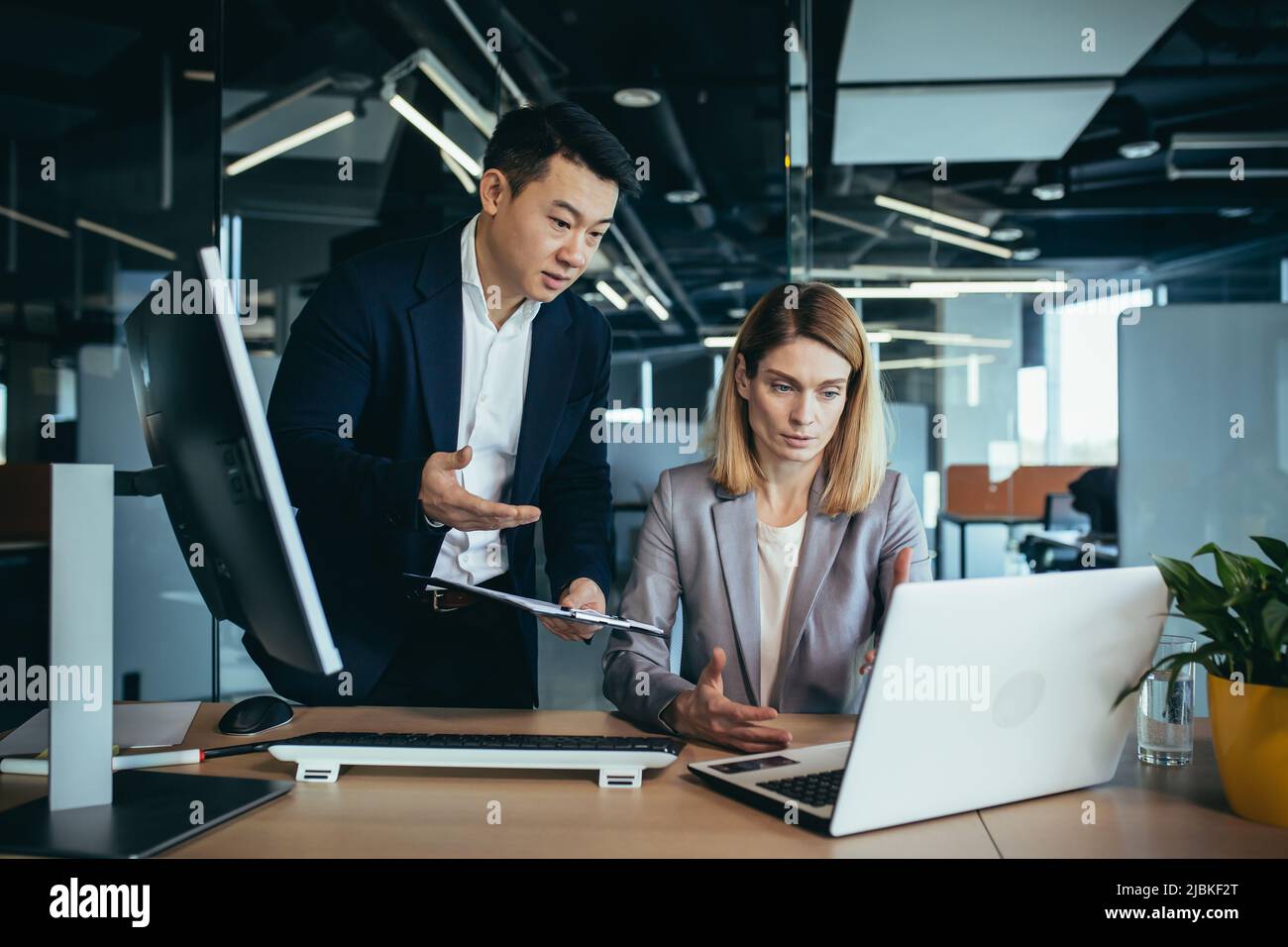 Two employees in a modern office, an Asian man and a woman working at a ...