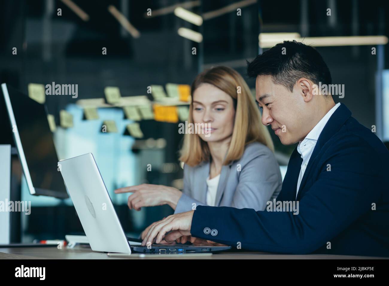 happy coworkers discuss project strategy by looking and pointing at laptop pc computer monitor ...
