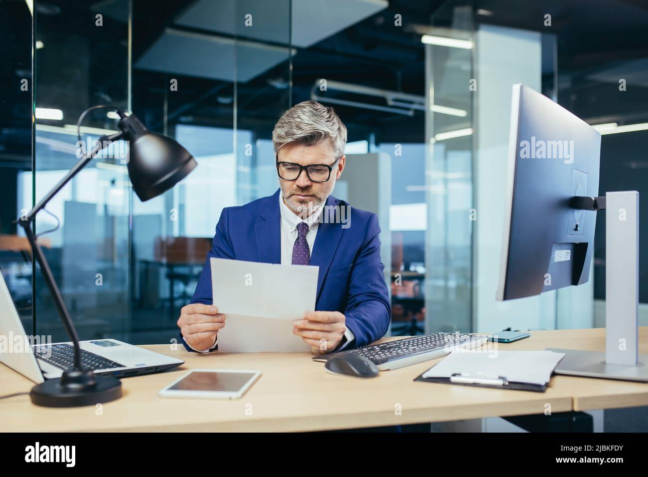 Experienced gray-haired businessman working at a computer, paperwork in ...