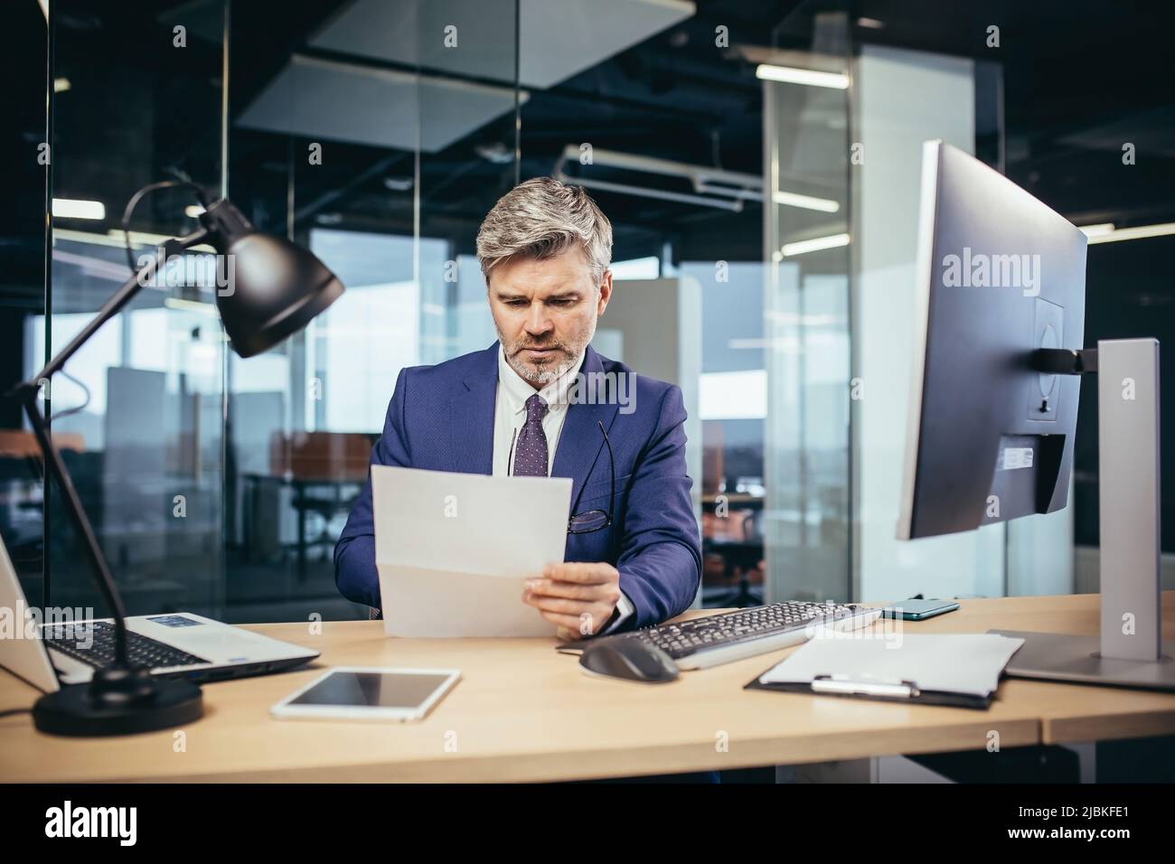 Experienced gray-haired businessman working at a computer, paperwork in ...