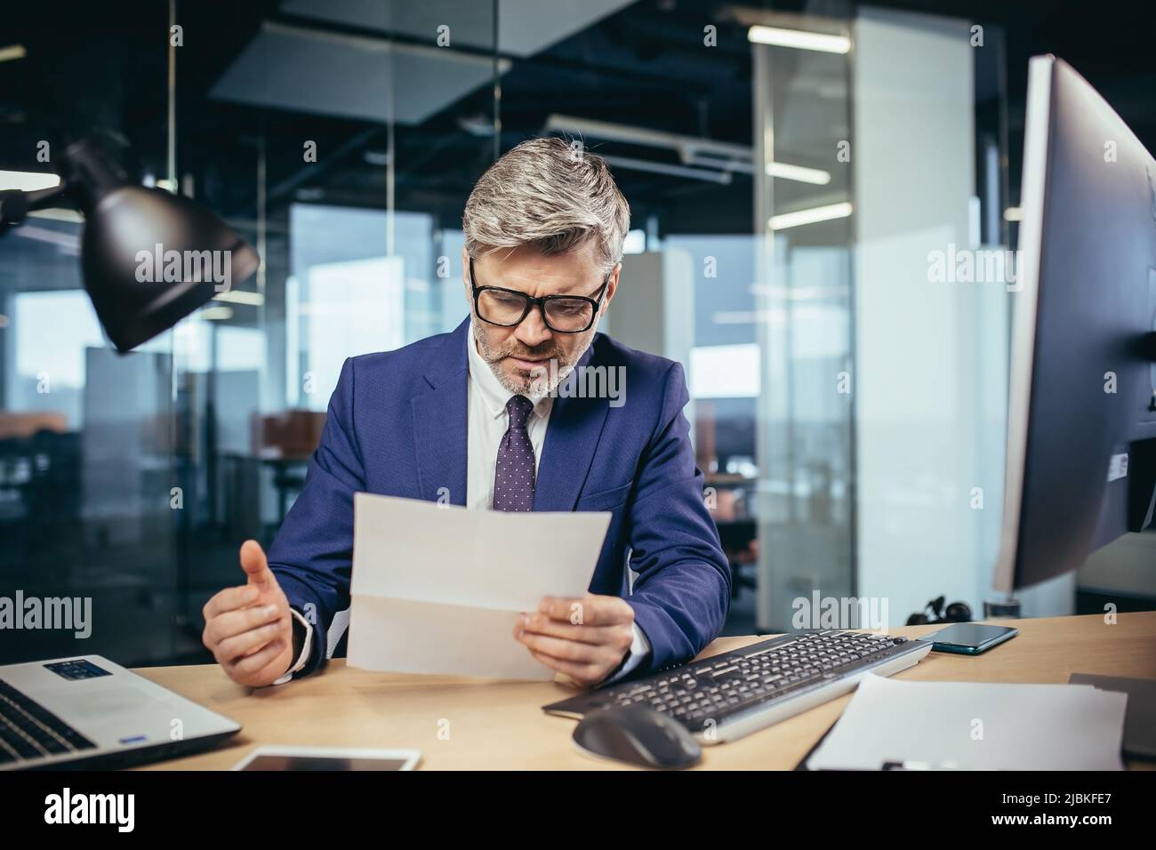 Experienced gray-haired businessman working at a computer, paperwork in ...