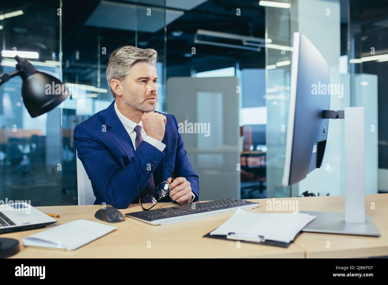Pensive boss working at computer in modern office, successful male ...