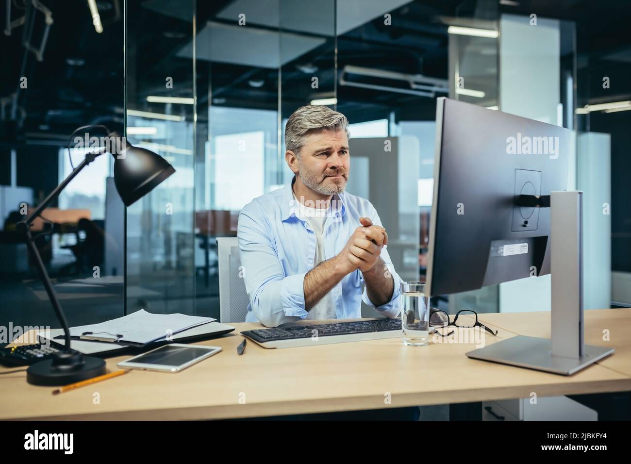 Senior and experienced businessman, looks frustrated at the monitor ...