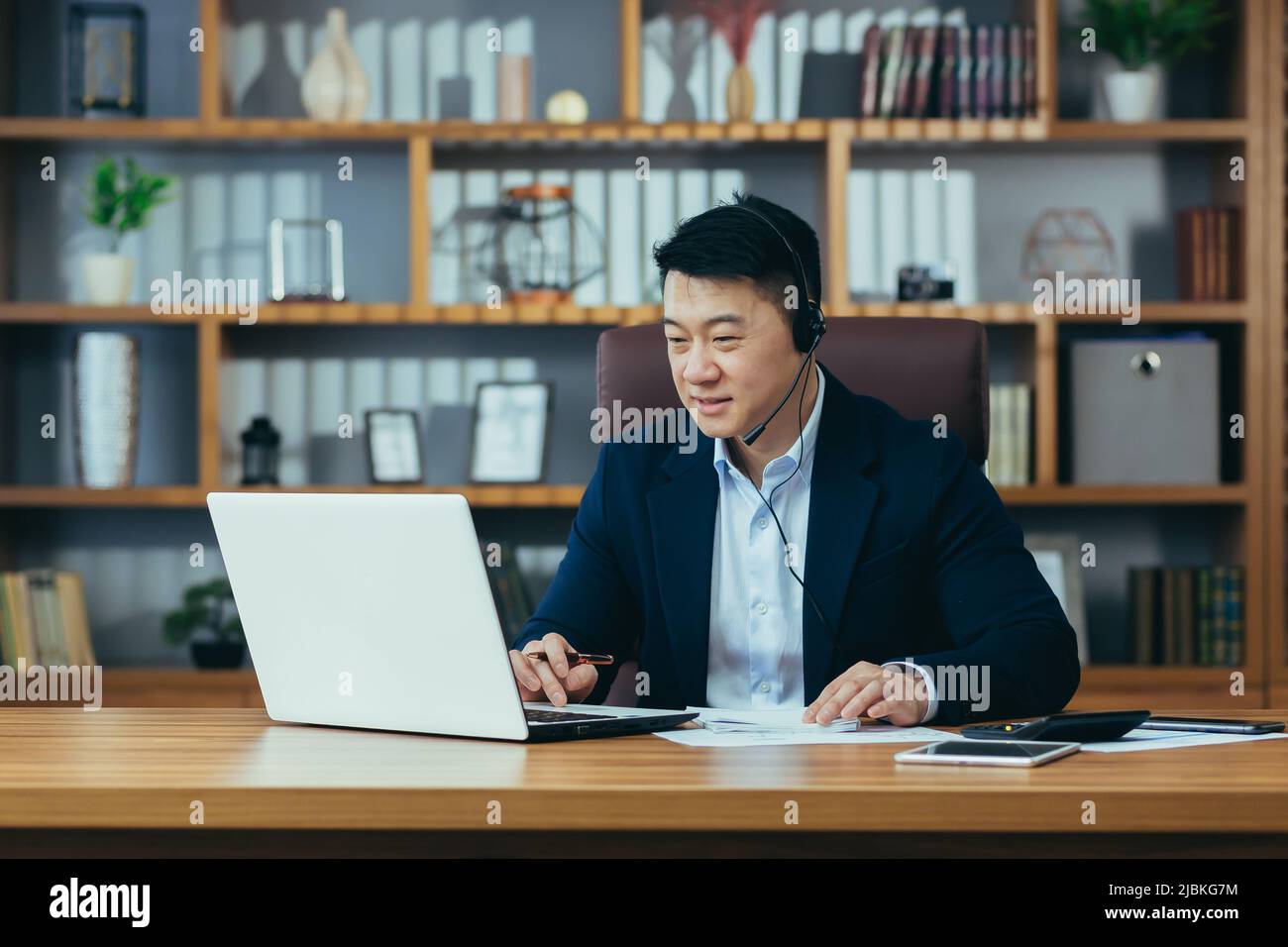 Asian business teacher teaches students online, uses headset and laptop ...