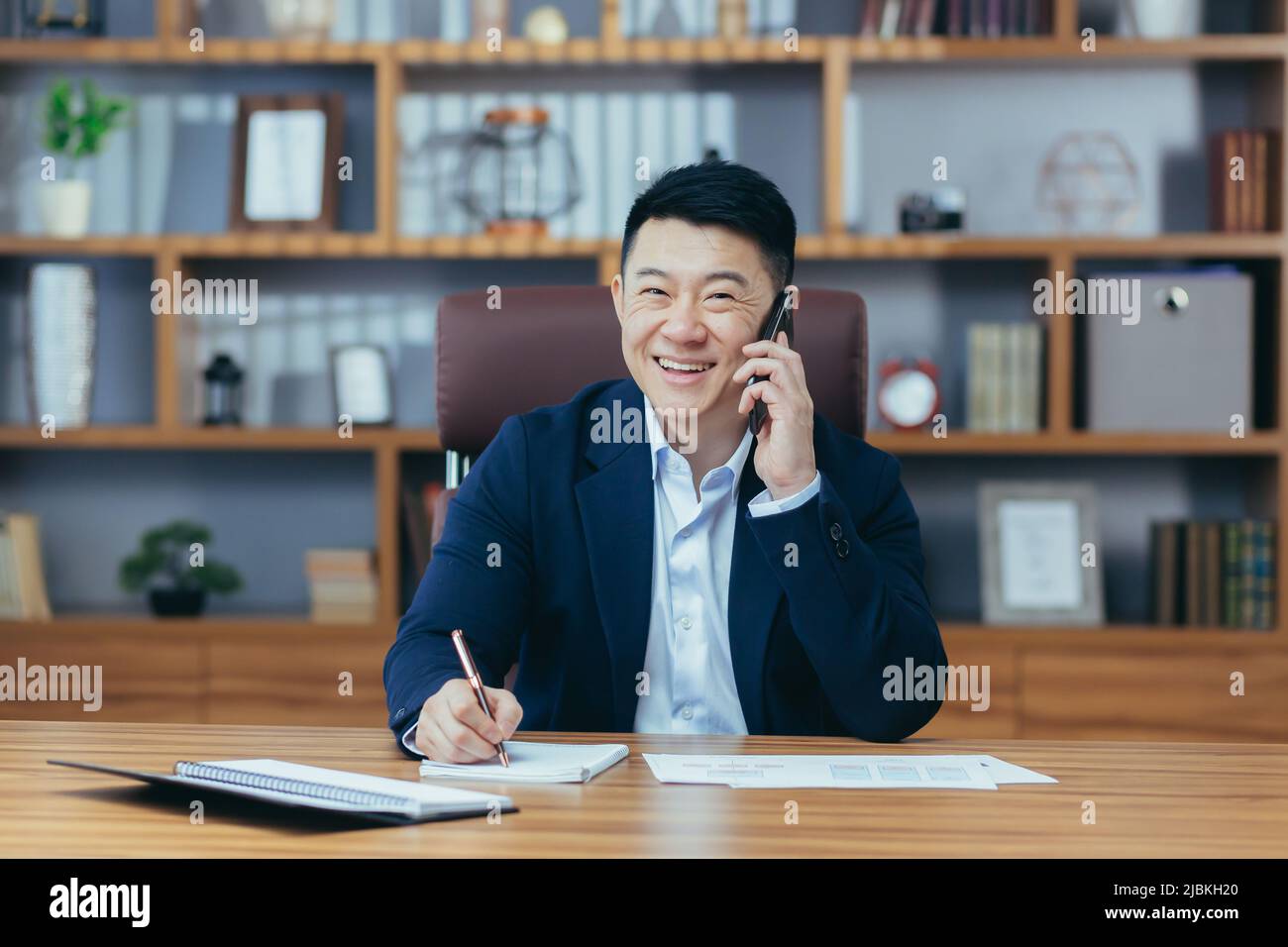Successful paper boss in office looks at camera and smiles, asian ...