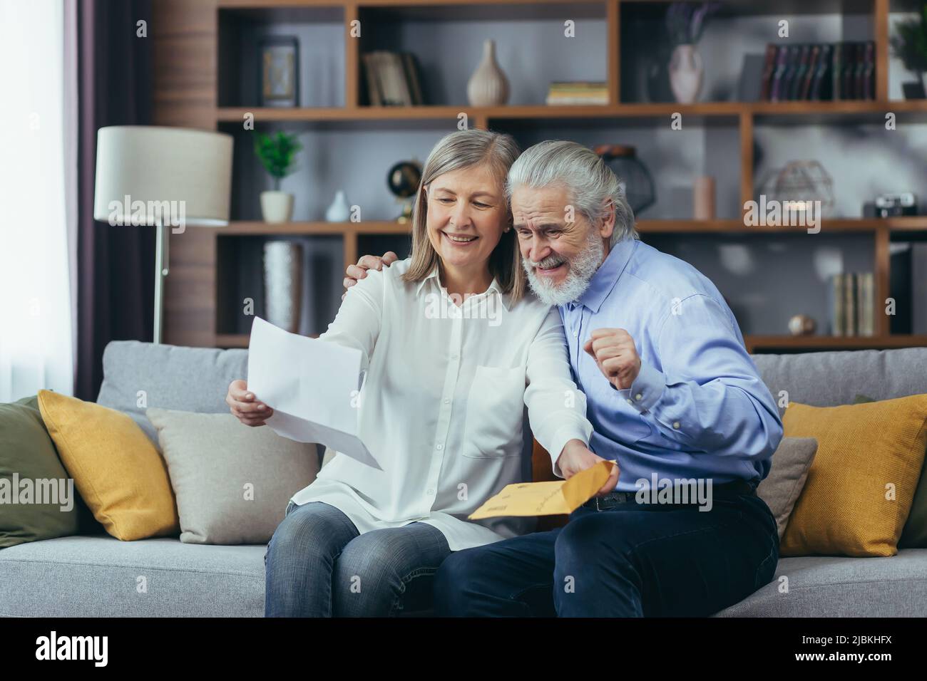 Happy senior retired couple sitting on sofa at home reading letter ...