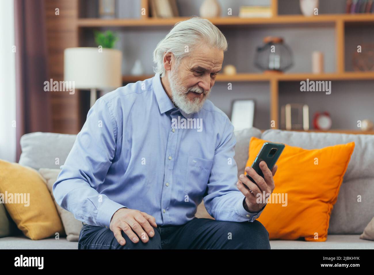 Senior man at home sitting on sofa looking at phone screen, talking on ...