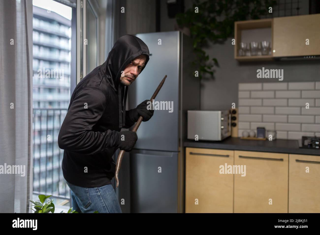 Young male robber in dark clothes carefully and quietly enters through ...