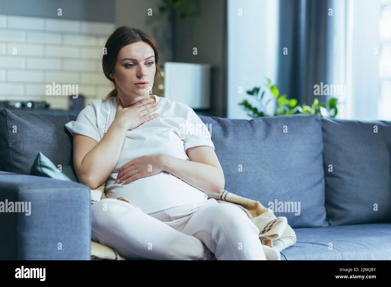 Pregnant woman at home sitting on the couch, nausea Stock Photo - Alamy