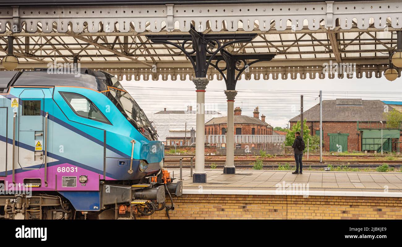 A modern locomotive rests at a railway station platform and a lone ...