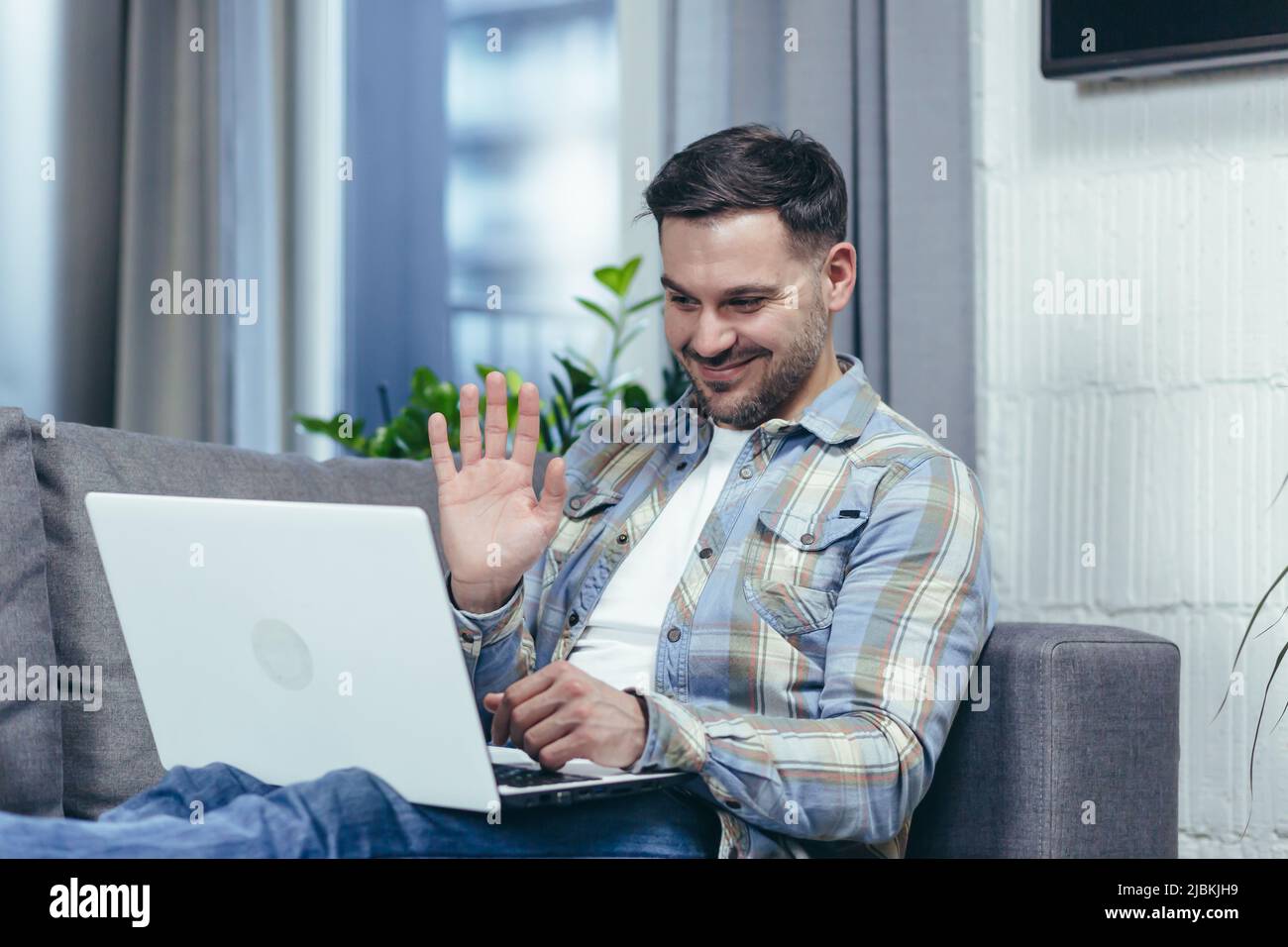 Man working at home sitting on sofa and talking on video call, looking ...