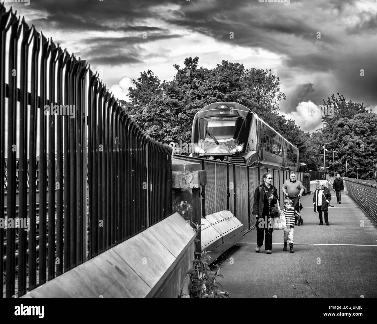 A train crosses a bridge above people on a footpath below. A fence is ...