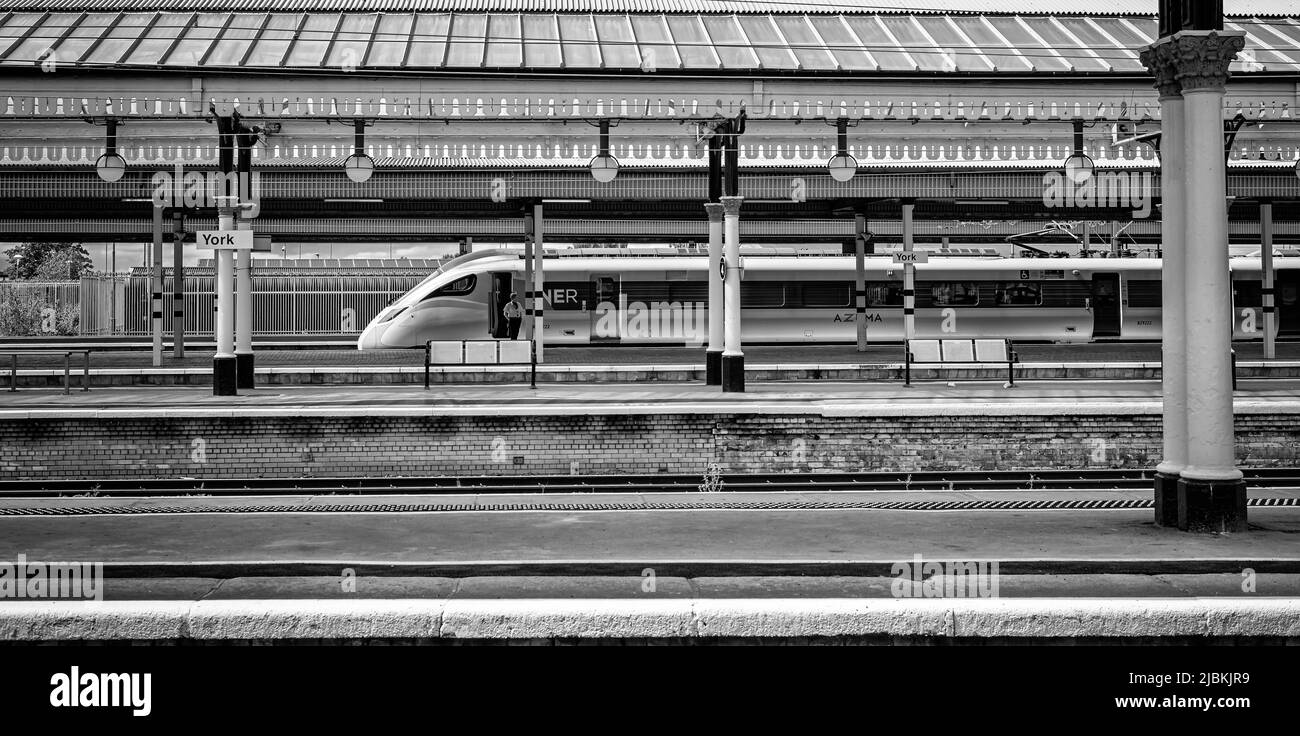 A sleek elongated modern train rests at a railway station platform. A ...