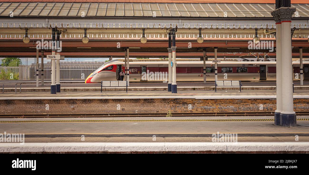 A sleek elongated modern train rests at a railway station platform. A ...