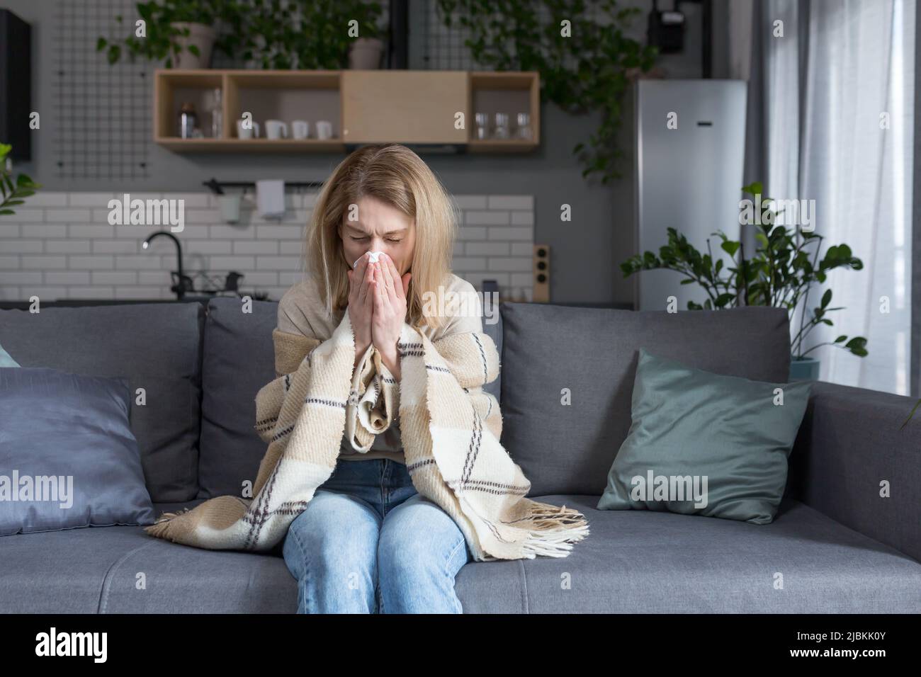 The sick woman is sitting on the couch at home, has a cough and fever ...