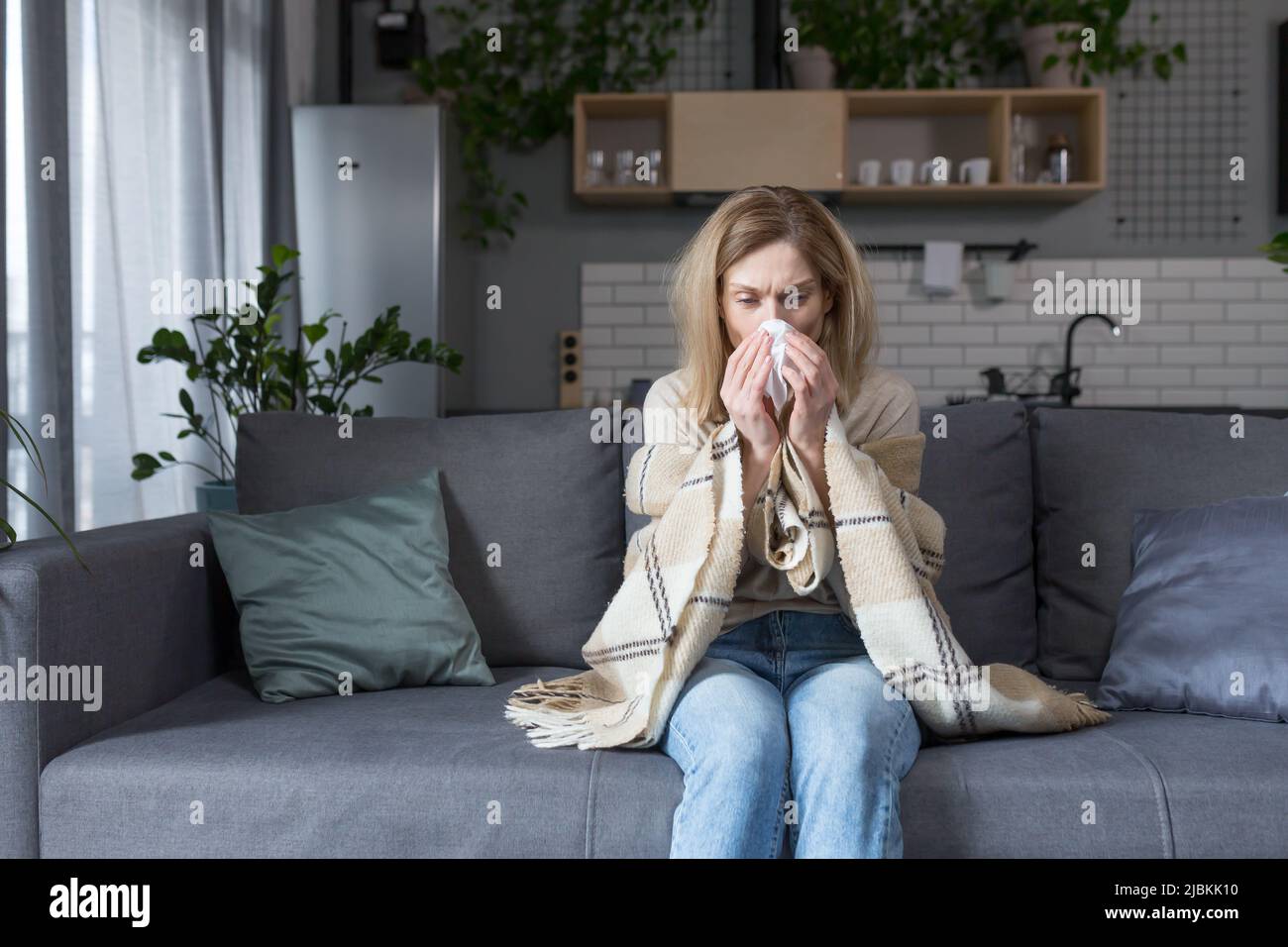 The sick woman is sitting on the couch at home, has a cough and fever ...