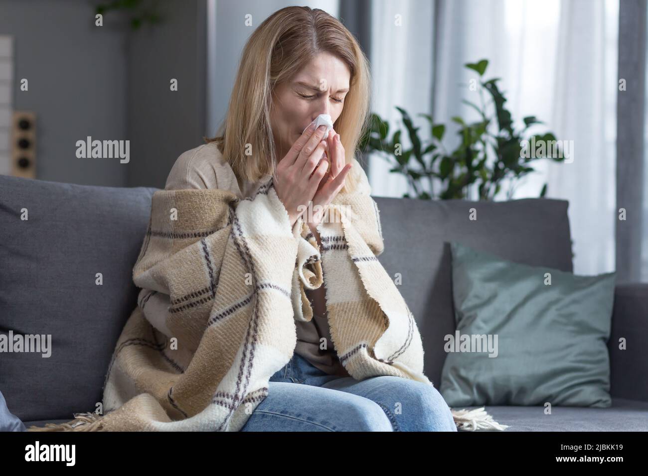 The sick woman is sitting on the couch at home, has a cough and fever ...