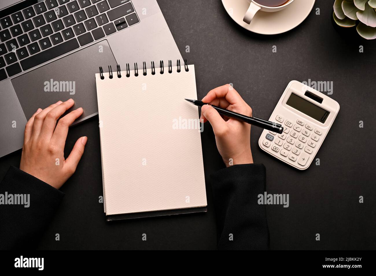 A female hand writing on blank spiral notepad in her modern black ...