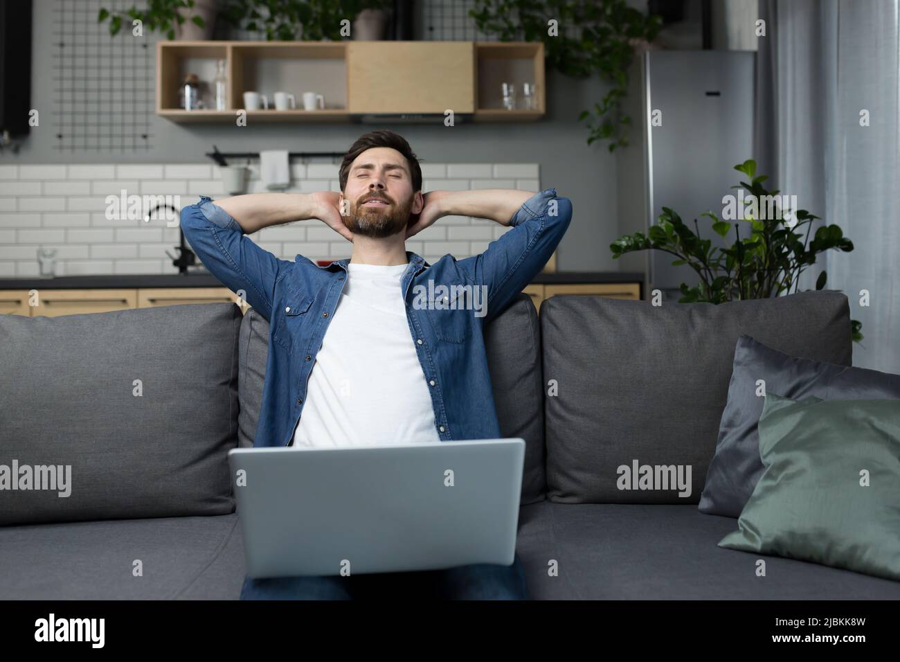 The man at home is resting while working on a laptop, sitting on the ...