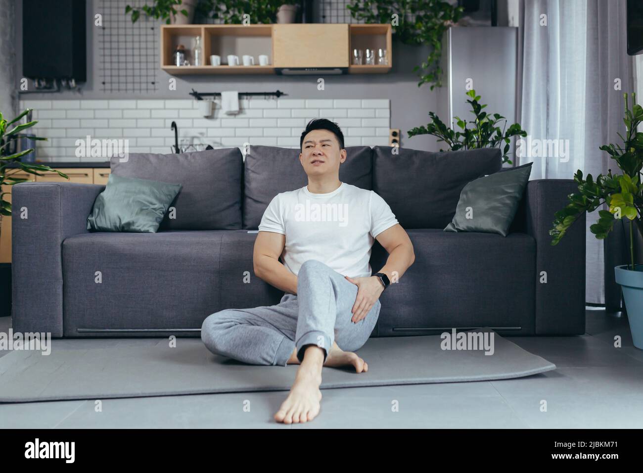 Asian Man in sportswear suffering from knee pain at home Stock Photo ...