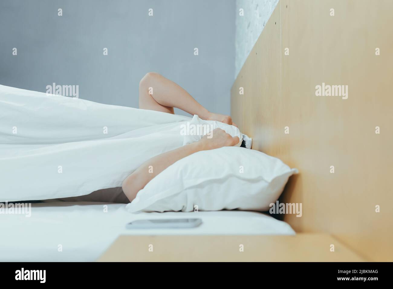 A sad Asian man lies in bed depressed under a blanket at home Stock ...