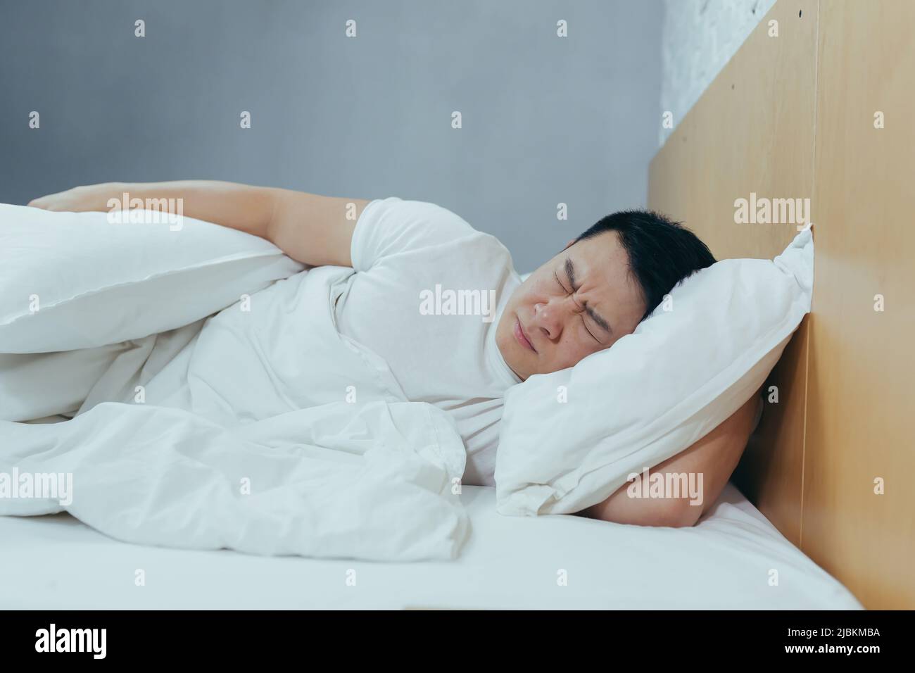 A sad Asian man lies in bed depressed under a blanket at home Stock ...