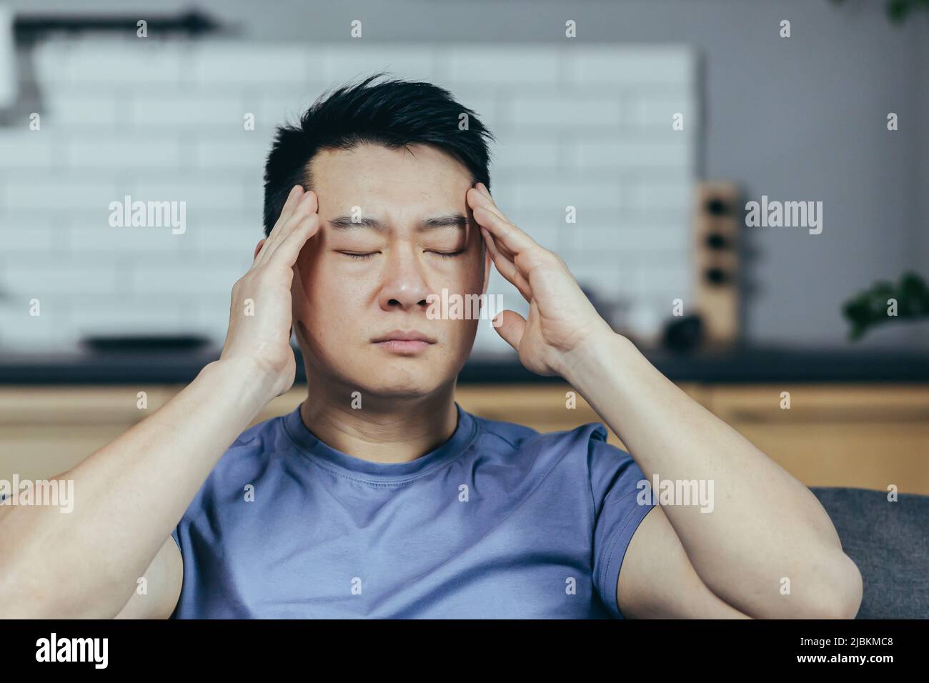 Tired and sick man at home alone, Asian has a headache, sits on the ...