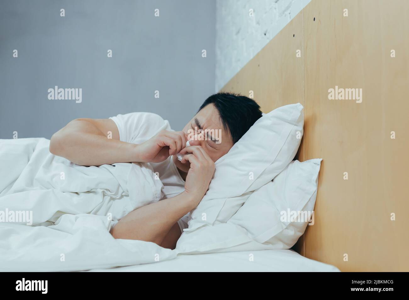 Sick man lying in bed has a runny nose cold and flu, Asian at home covered with a blanket Stock ...