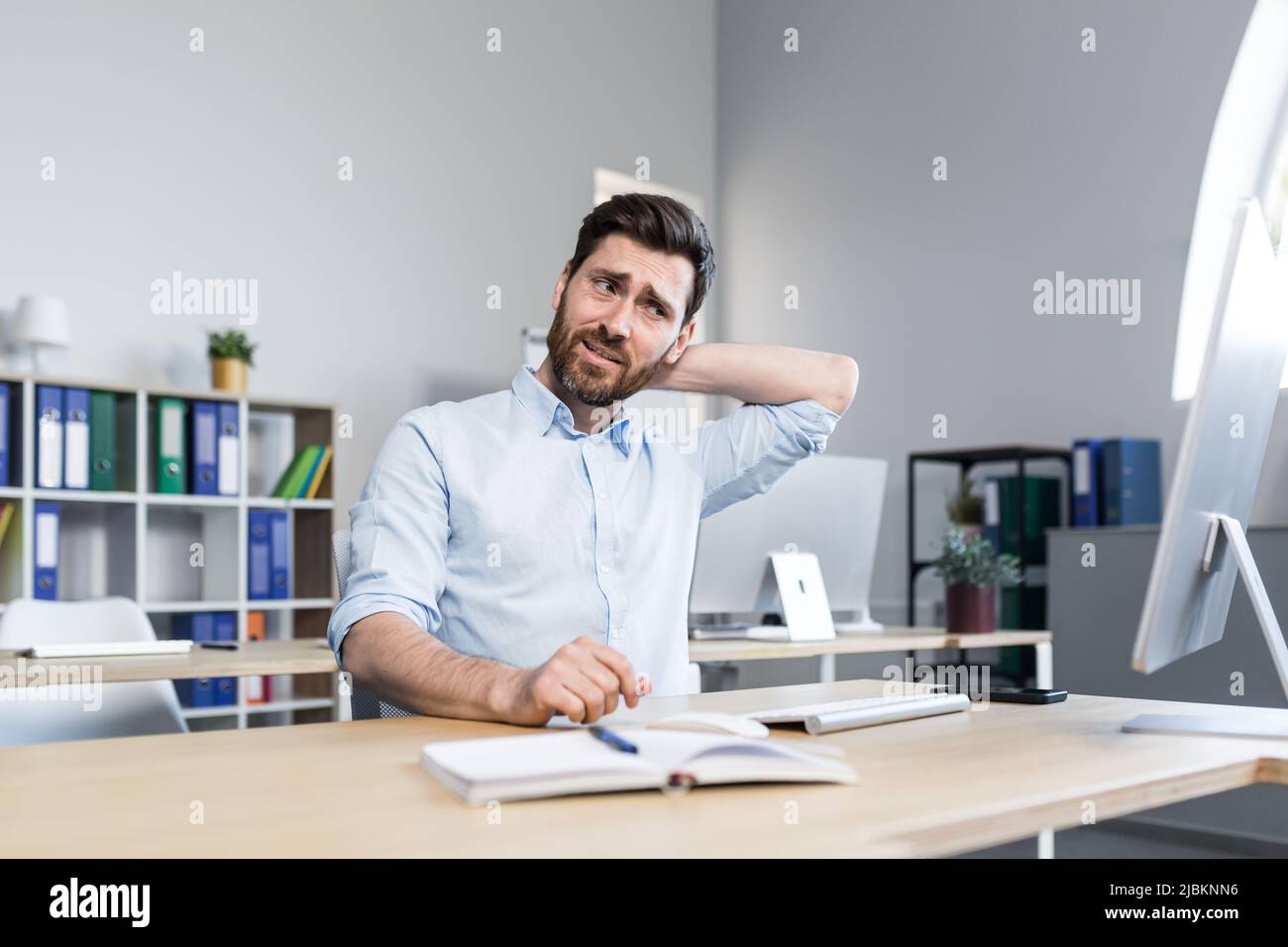 A tired young man working at a computer and sitting at a desk in the ...