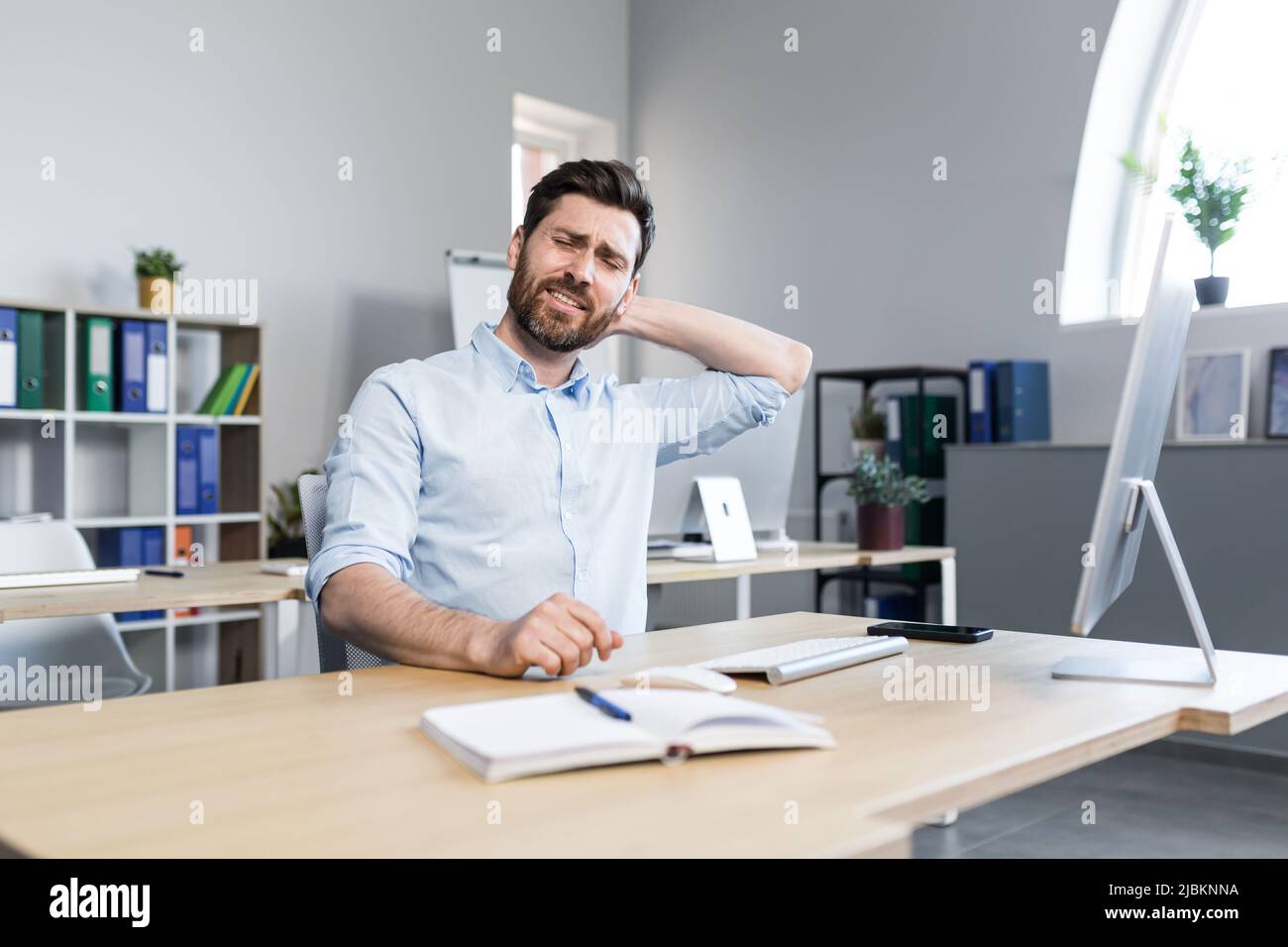 A tired young man working at a computer and sitting at a desk in the ...