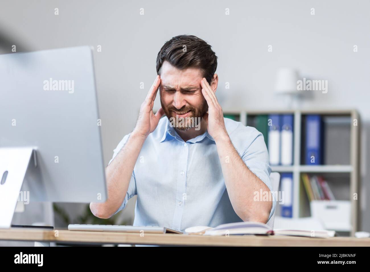 Tired and annoyed young man, office worker, manager holding his head ...