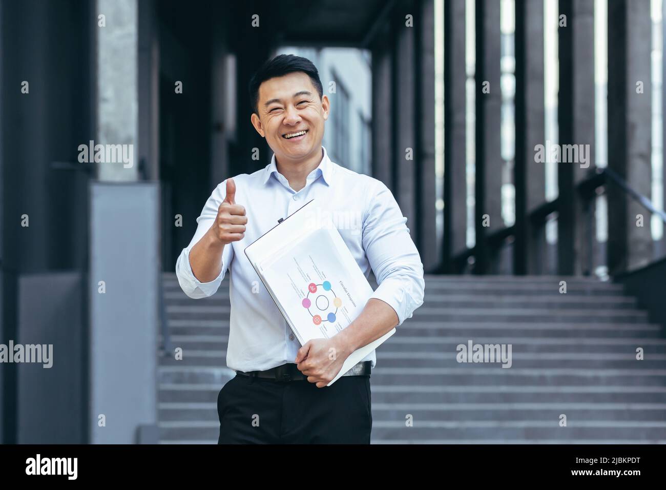 Portrait of Asian businessman broker, man outside office holding laptop ...