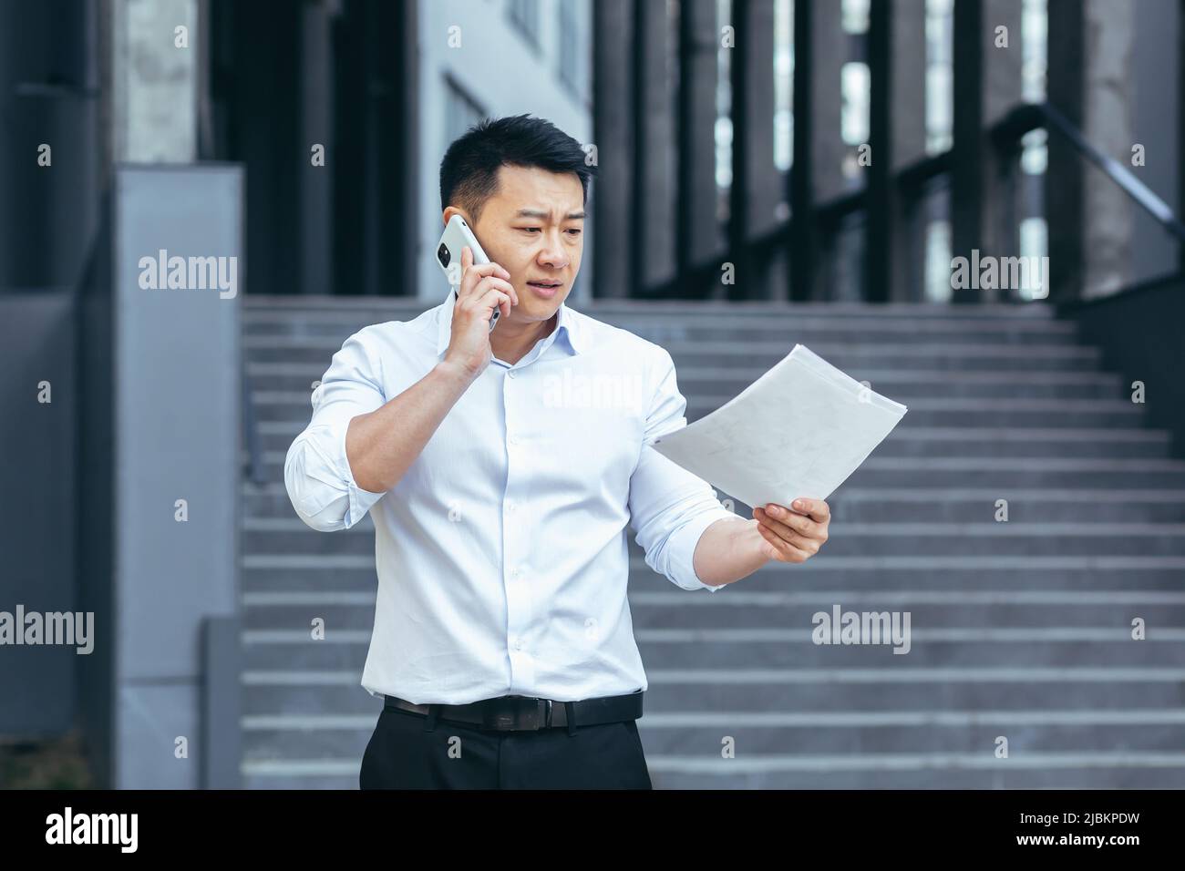 Frustrated insurance agent with documents talking on the phone outside ...