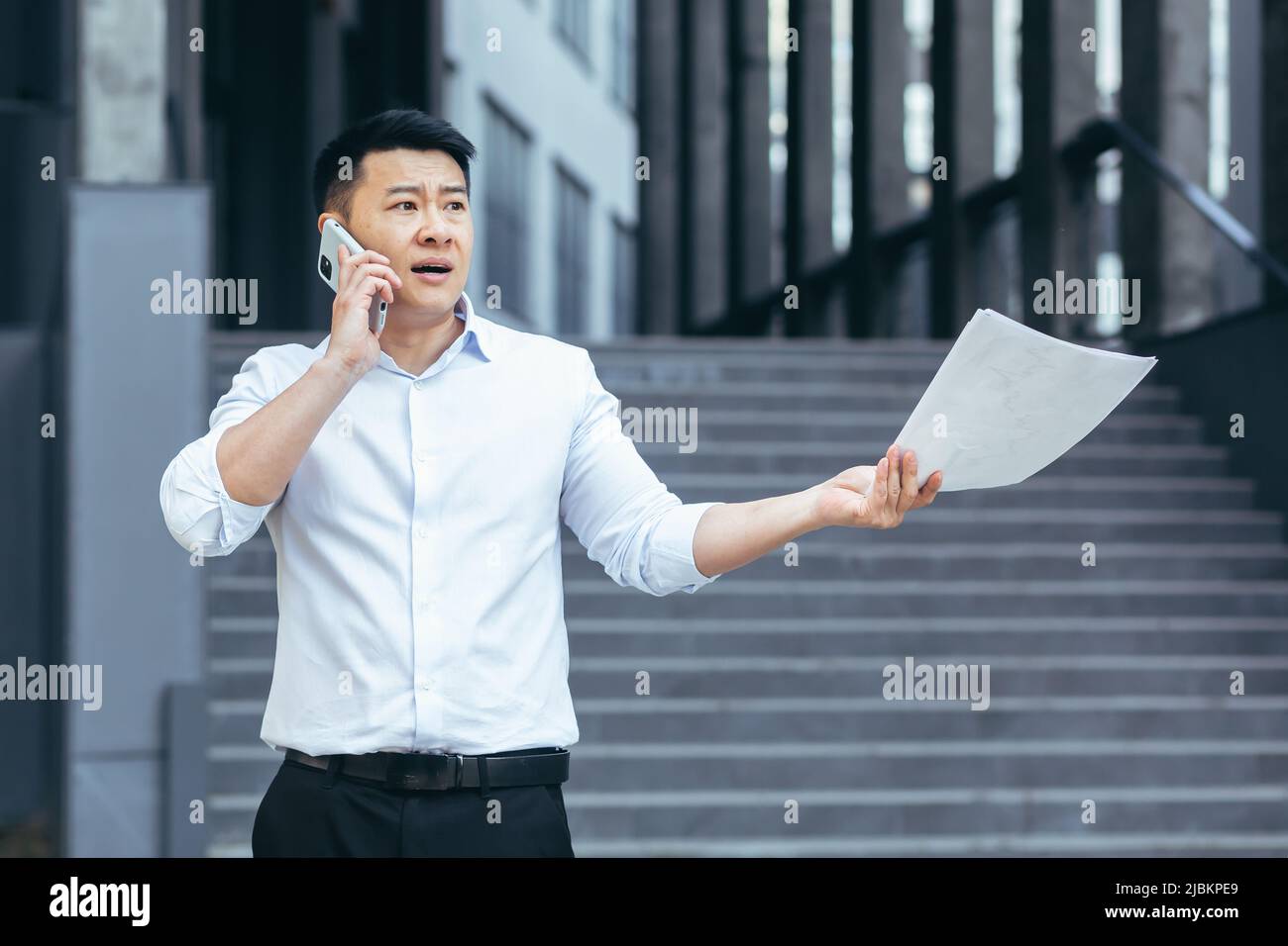 Frustrated insurance agent with documents talking on the phone outside ...