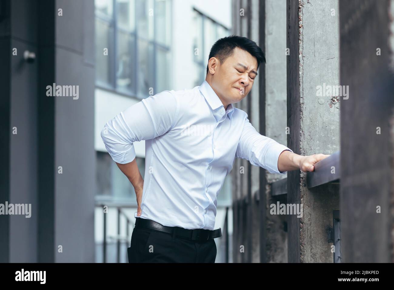 Tired asian businessman near office, doing back massage, has severe ...