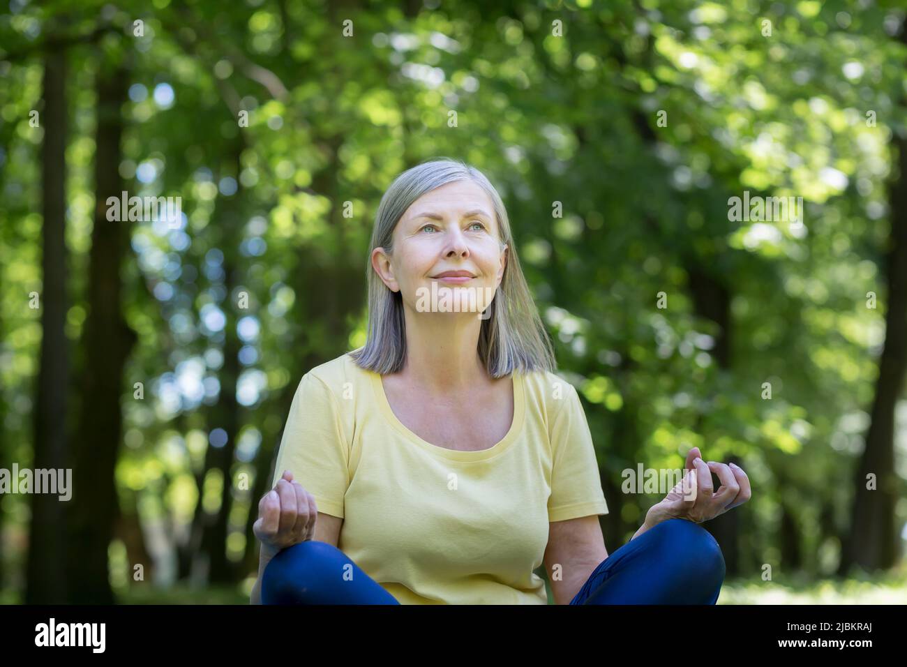 Senior gray-haired retired woman in the park meditates and performs ...