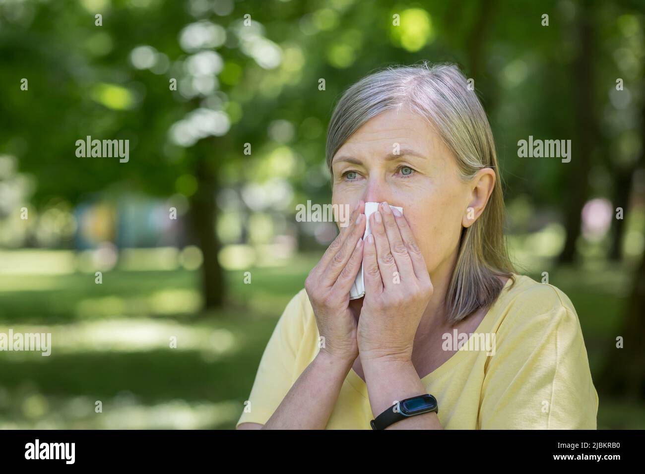 An elderly woman in the park with allergies has a runny nose and ...