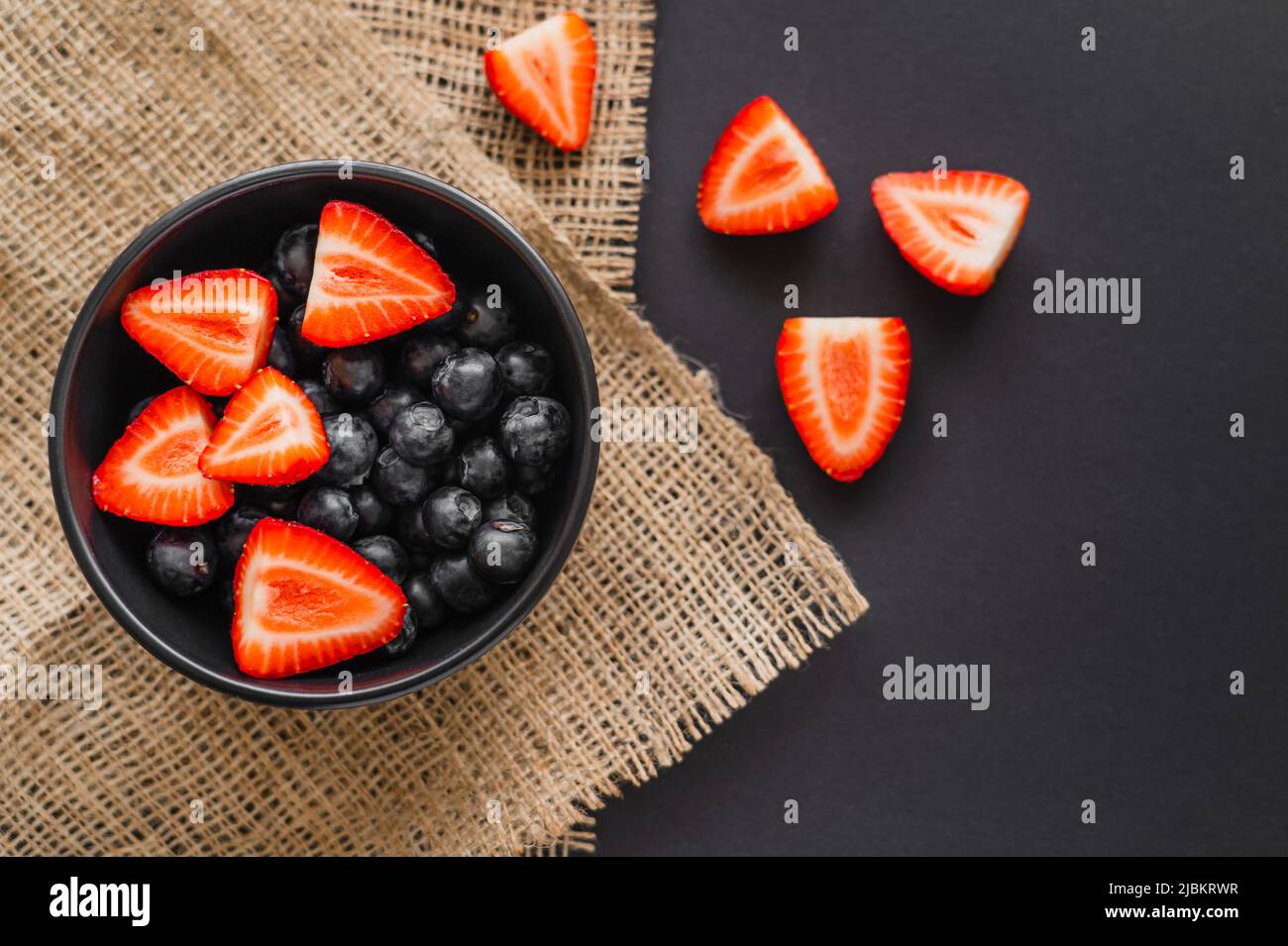 Top view of natural berries in bowl on sackcloth on black background ...