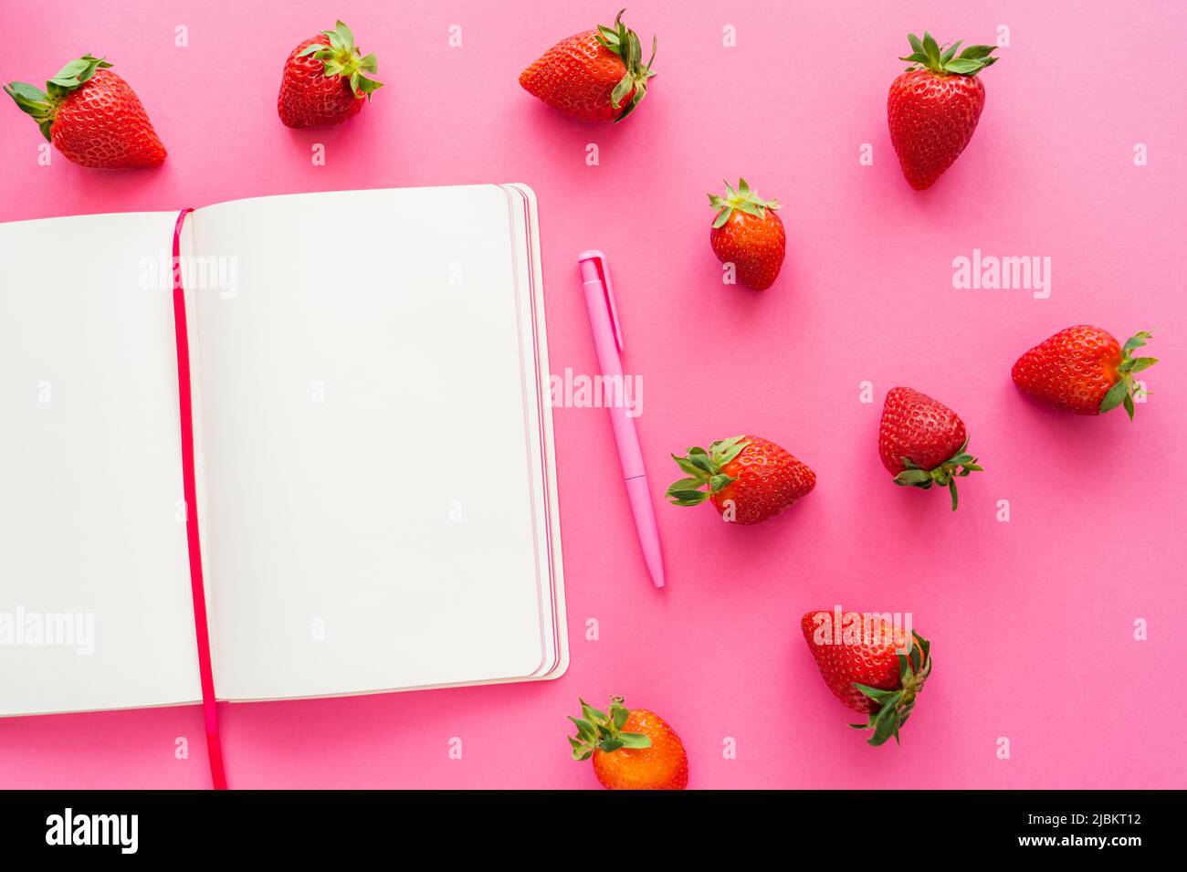 Top view of organic strawberries and open notebook on pink background ...