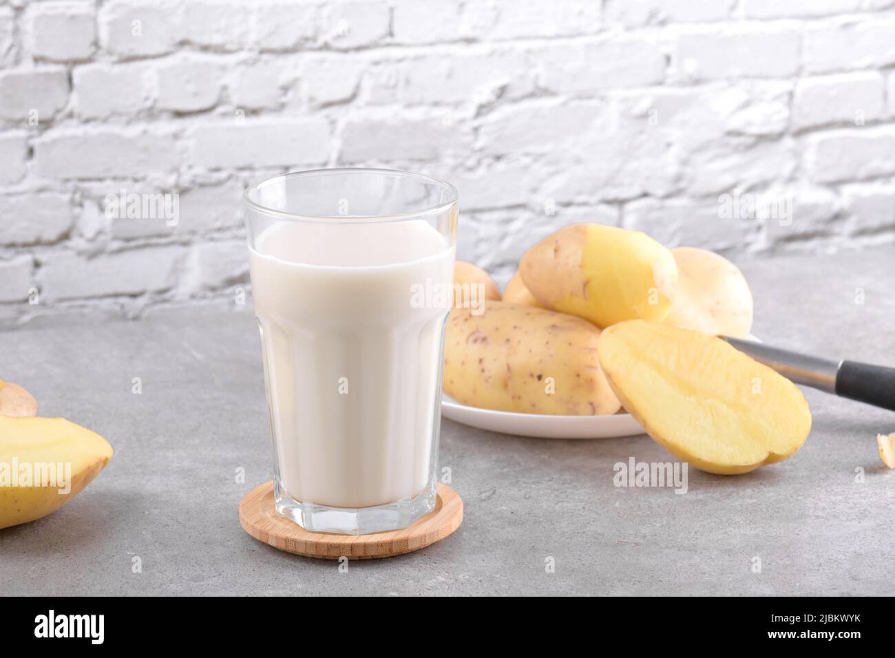 Vegan potato milk in a glass and potato tubers on grey stone table ...