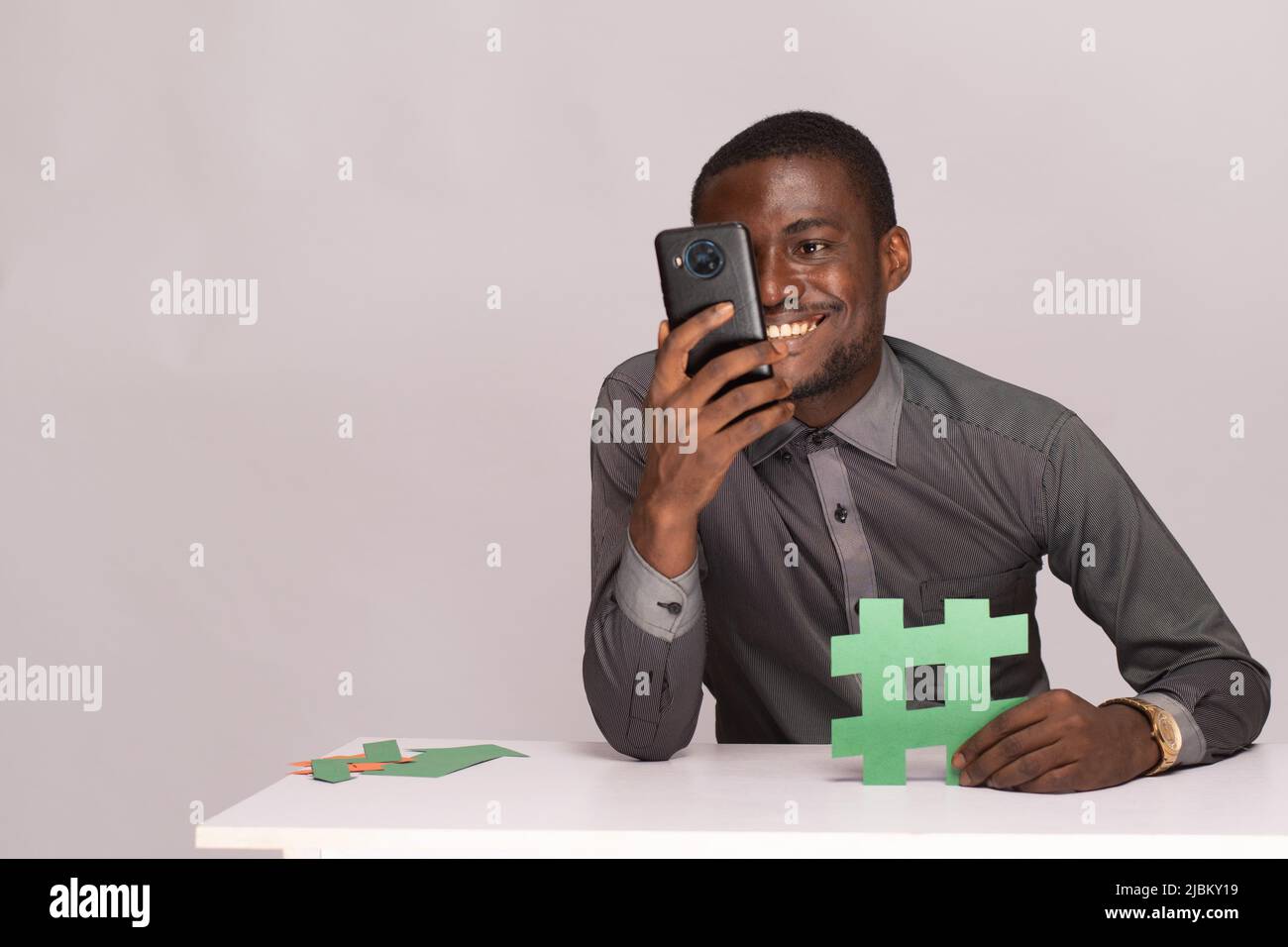 black man holding a hash tag symbol and phone smiling Stock Photo - Alamy