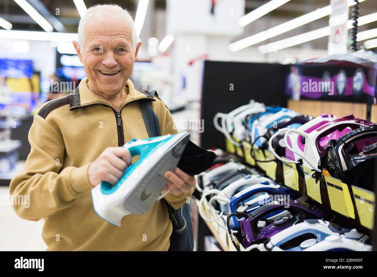 elderly man choosing iron in showroom of electrical appliance store ...