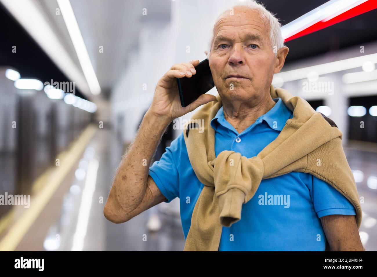 Elderly man using mobile phone while waiting for train in platform of ...