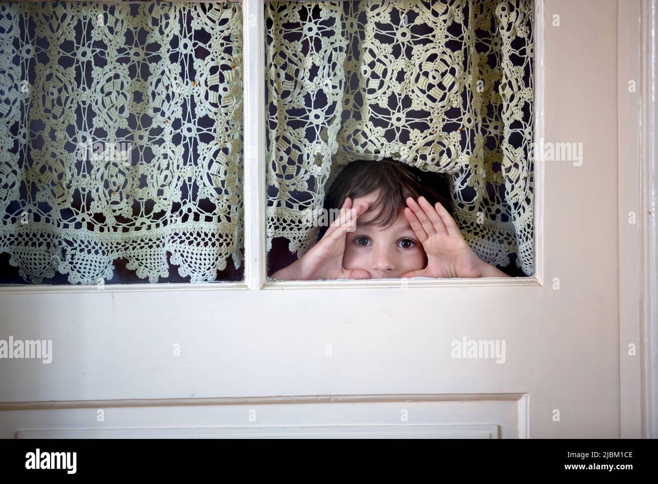 Little preschool boy, child, looking out scared through a door with ...
